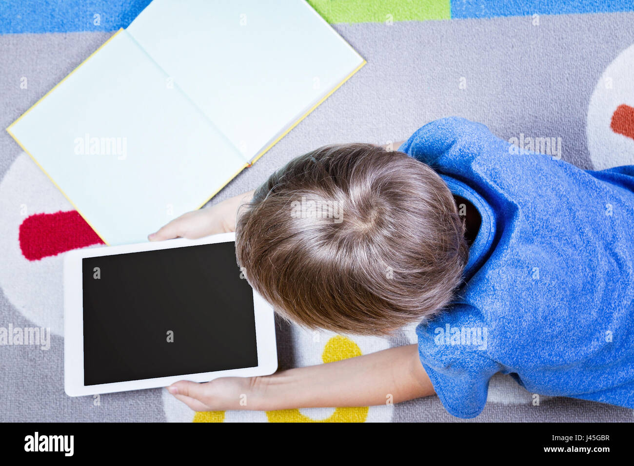 Boy looking at tablet pc, lying on the floor with books Stock Photo - Alamy