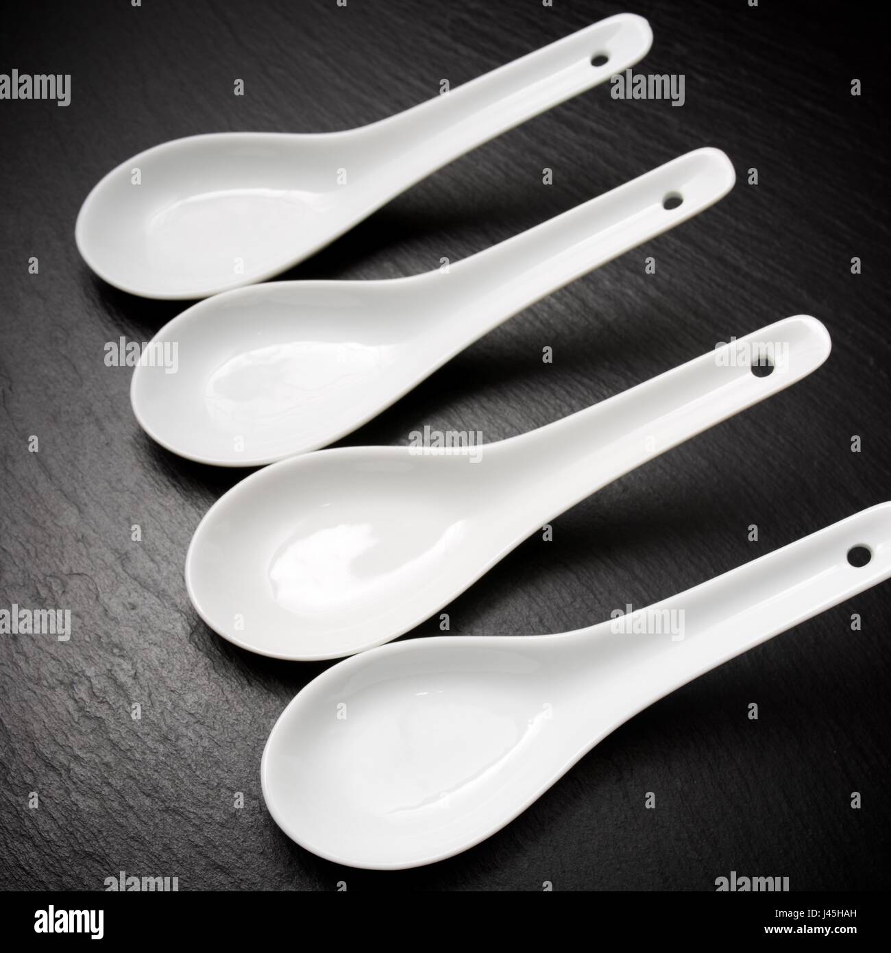 four small white spoons on a table slate Stock Photo - Alamy