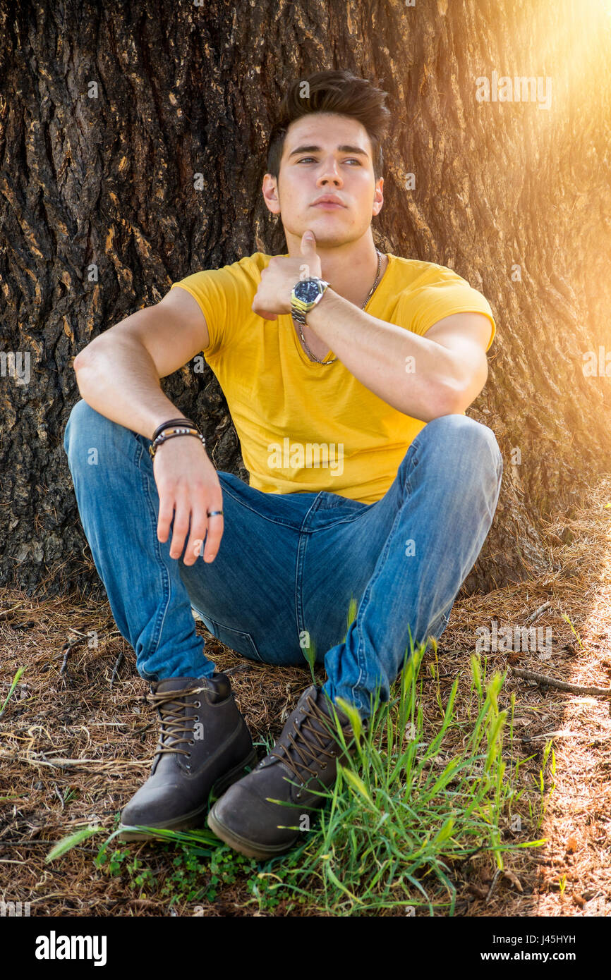Attractive young man in park resting against tree Stock Photo - Alamy