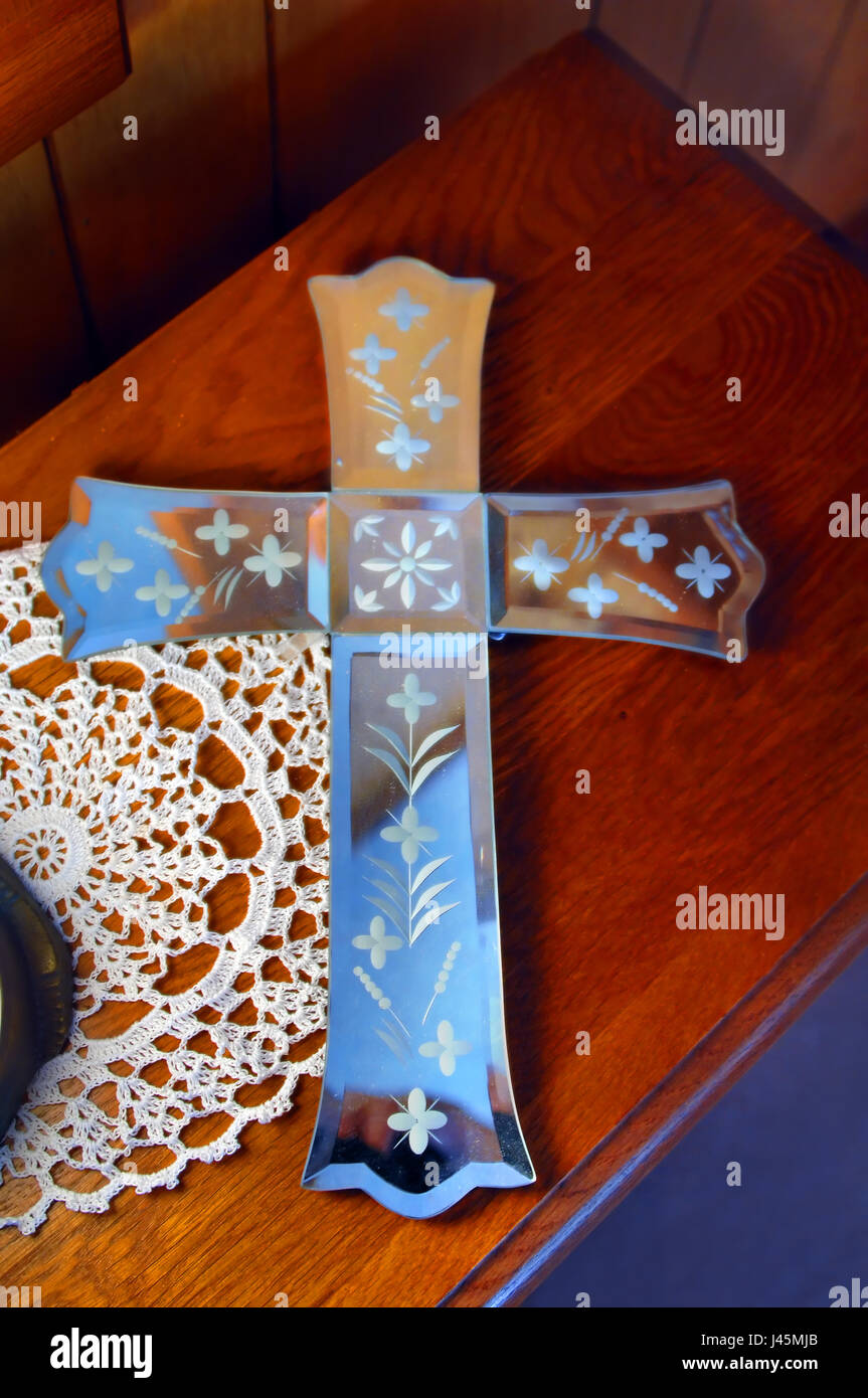 Mirror and glass cross, with etched flowers, lays on an end table in a ...