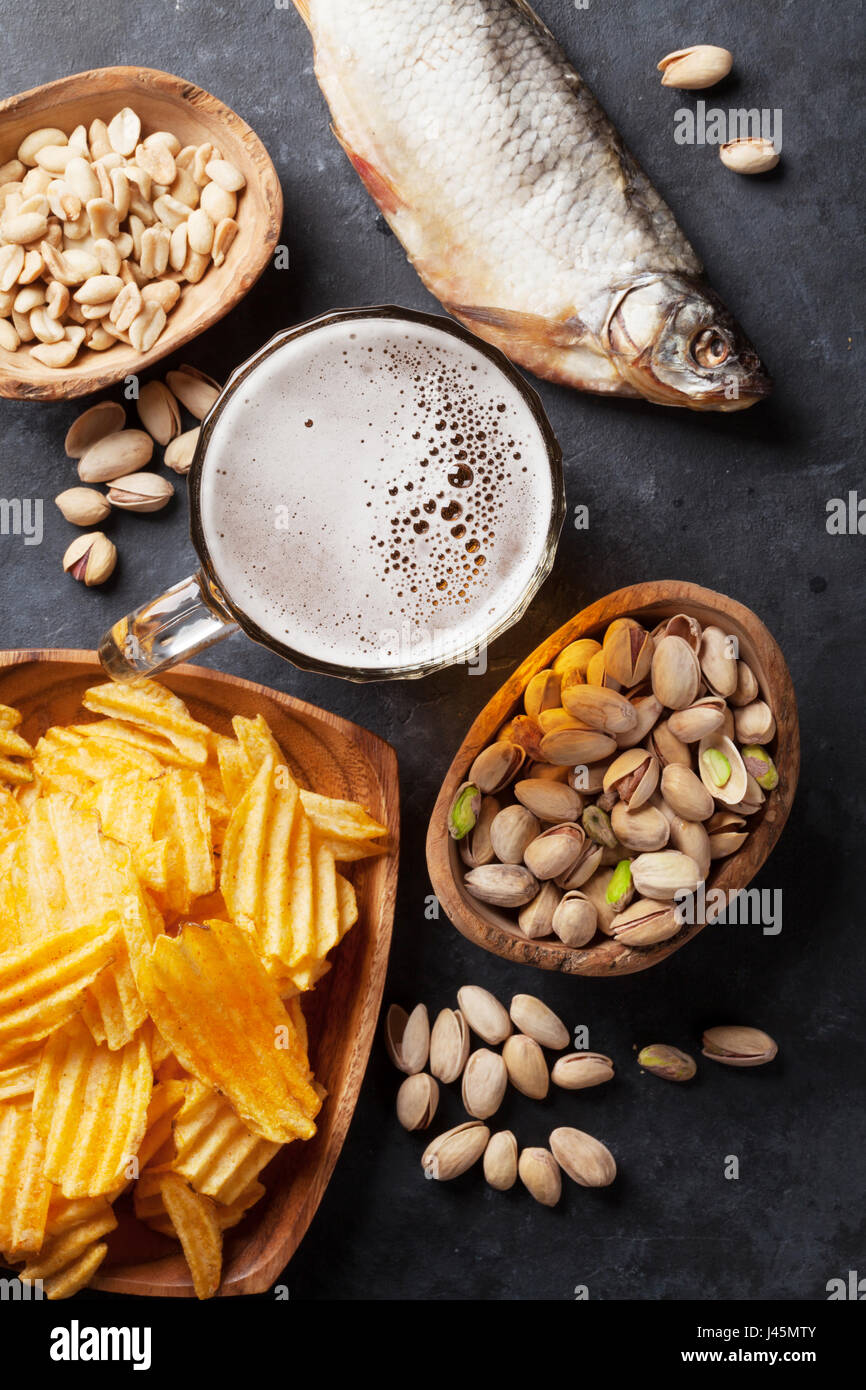 Lager beer and snacks on stone table. Nuts, chips, dry fish. Top view ...