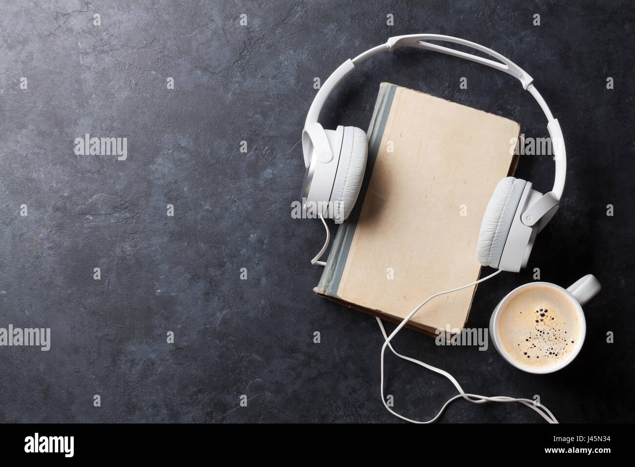Audio book concept. Headphones, coffee and old book over stone table ...