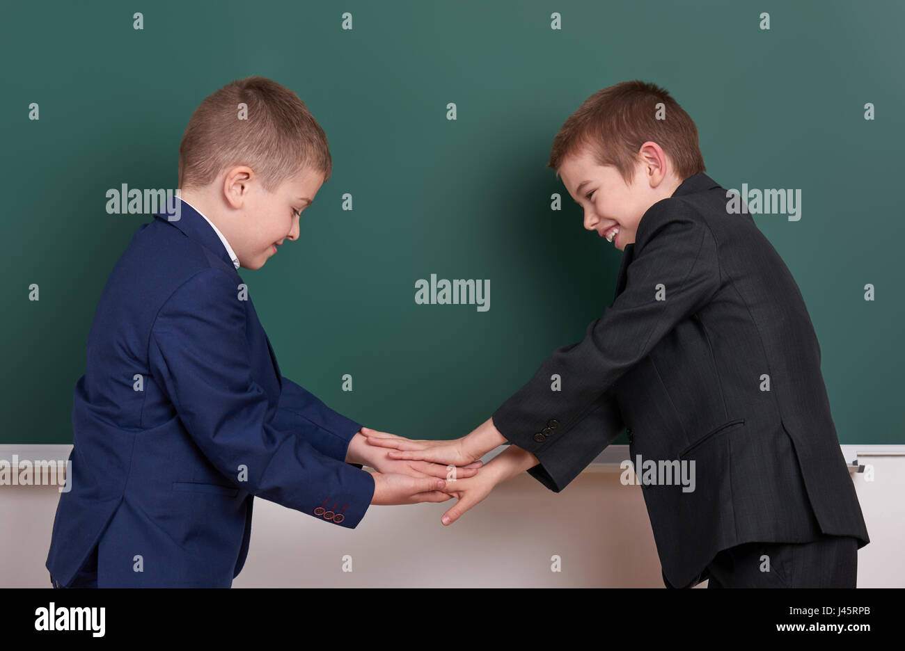 two friends handshake, elementary school boy near blank chalkboard ...