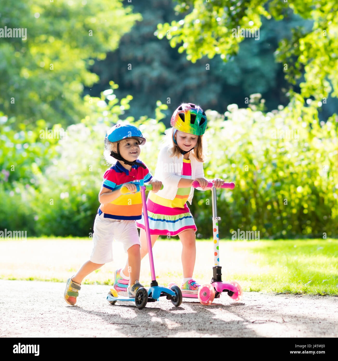 Children learn to ride scooter in a park on sunny summer day ...