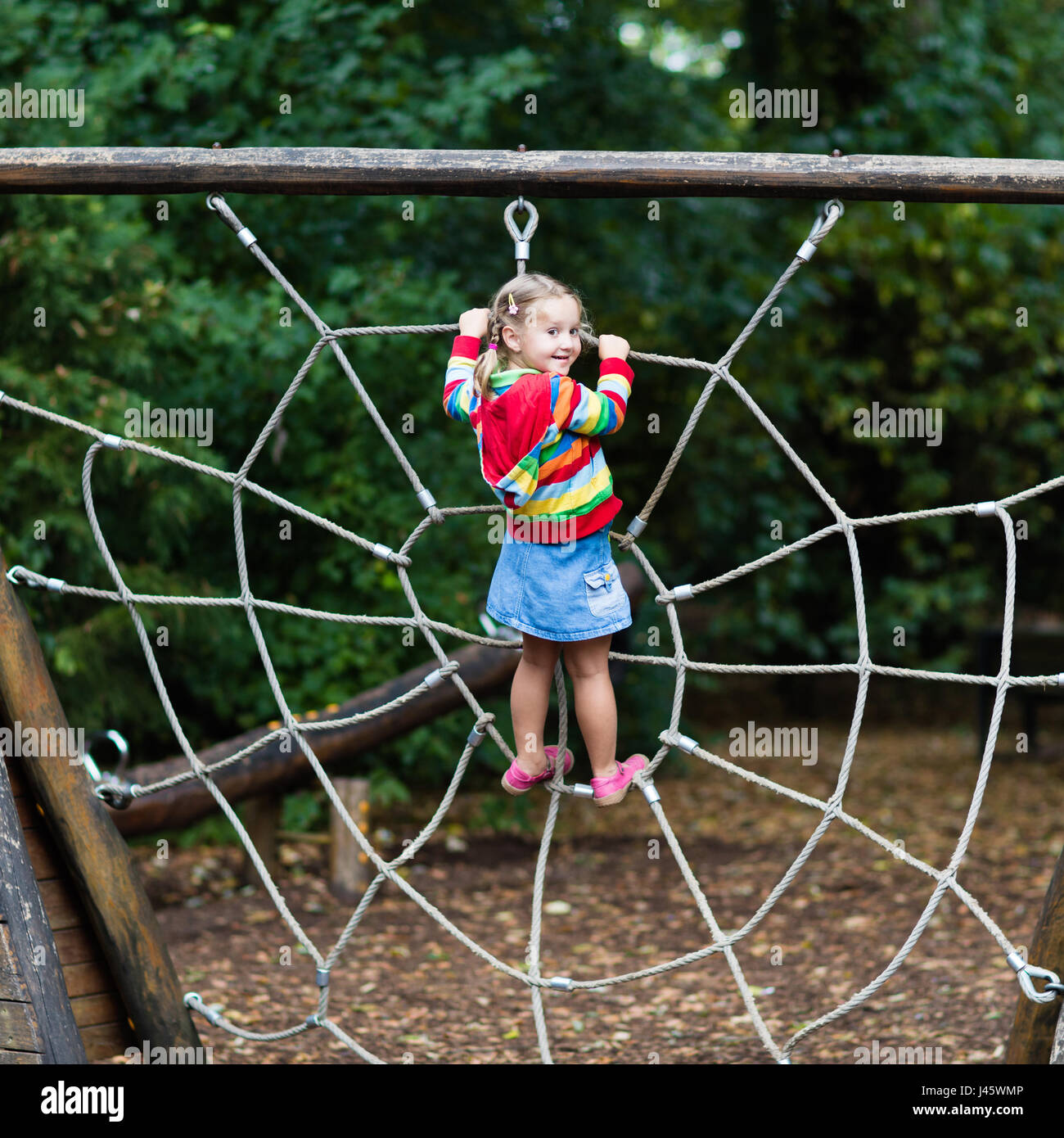 Active little child playing on climbing net and jumping on trampoline ...