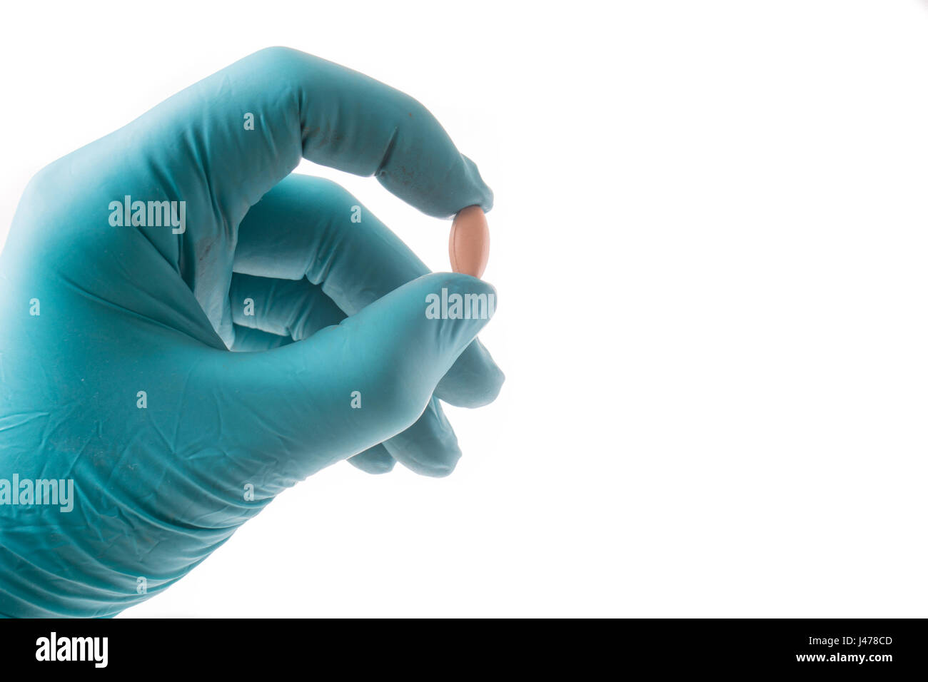Hand with green protective glove holding an oblong pill, isolated on ...