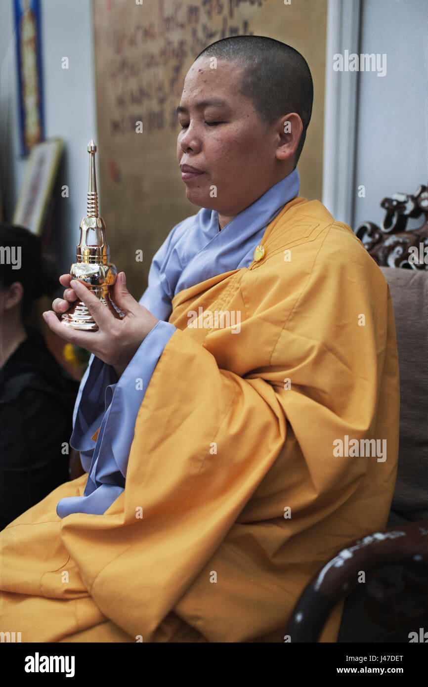 Buddhist nun with a shaved head wearing a yellow robe praying inside a ...