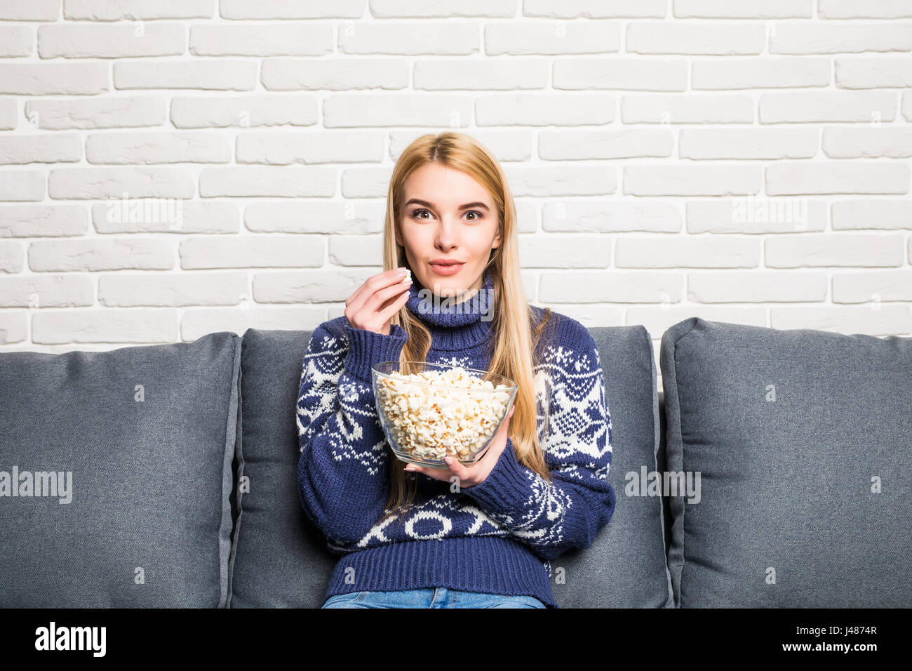 Portrait of beautiful young woman eating popcorn while watching film in ...