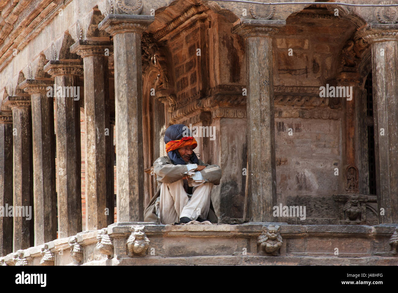 Man in traditional Nepali clothes sitting under the stone arches of ...