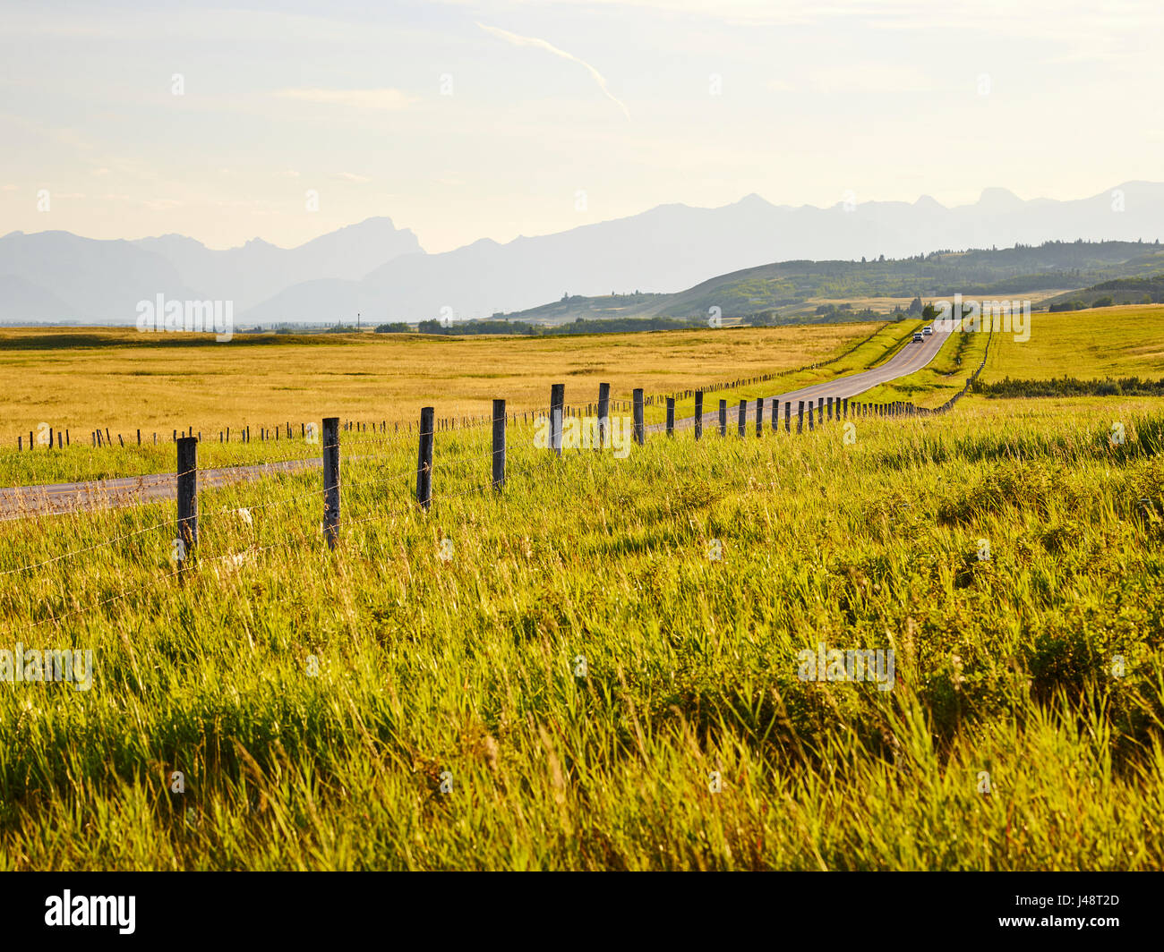 A country road between green fields and a silhouette of mountains in ...