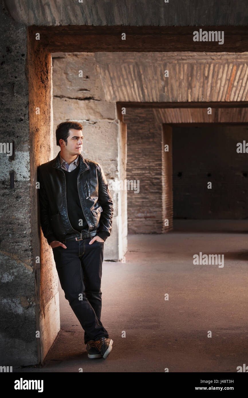 Portrait of a young man standing against a wall with concrete facade ...