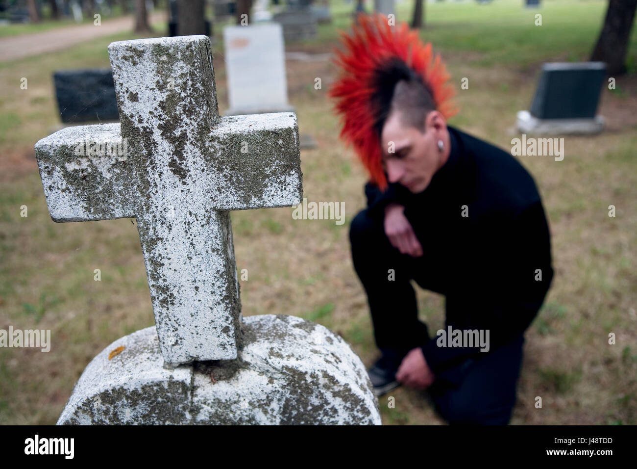 A Young Man With A Red Mohawk Grieves At A Tombstone In A Cemetery ...