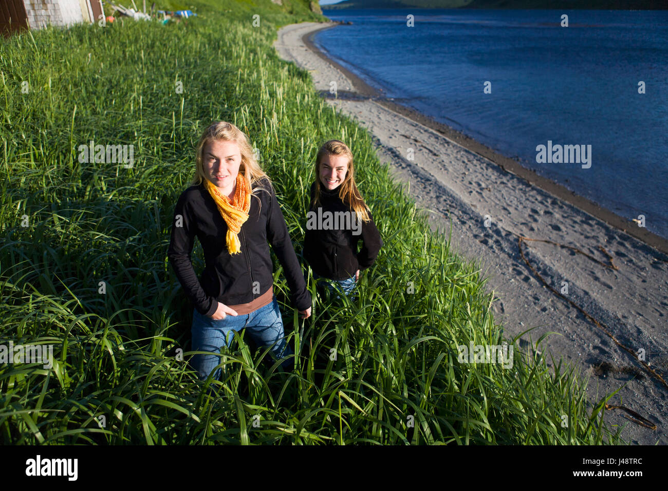 Two Sisters Stand Together In The Tall Grass At The Water's Edge; False ...