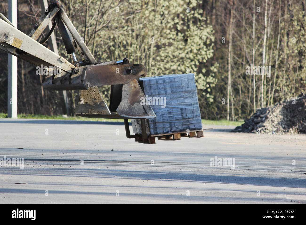 Tractor loader carries pallets with paving tiles across the road Stock ...