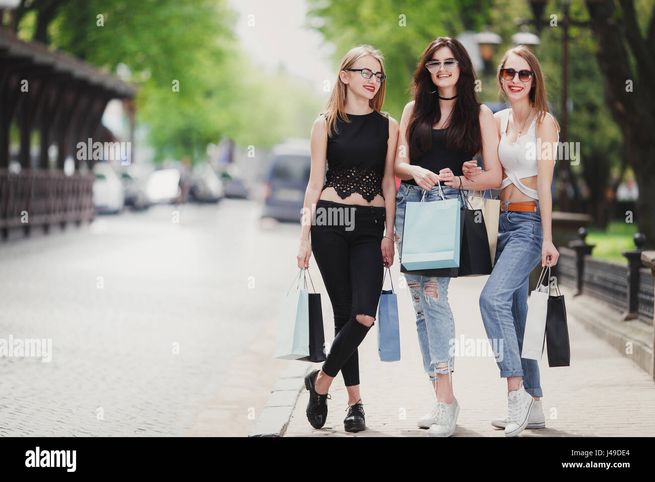 Three girls with shopping bags on park blur background Stock Photo - Alamy