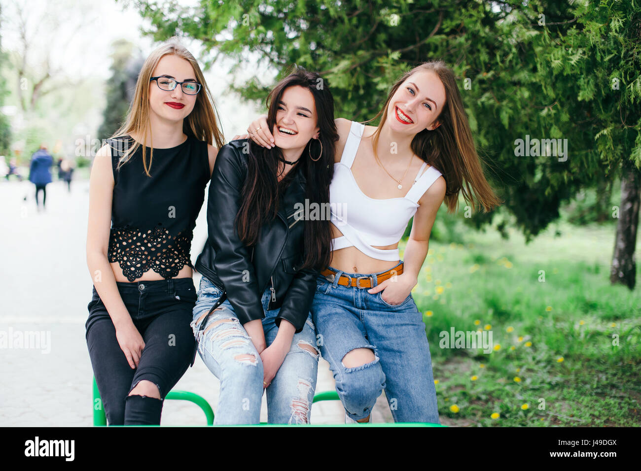 Three girls sit on the bench with on park blur background Stock Photo ...