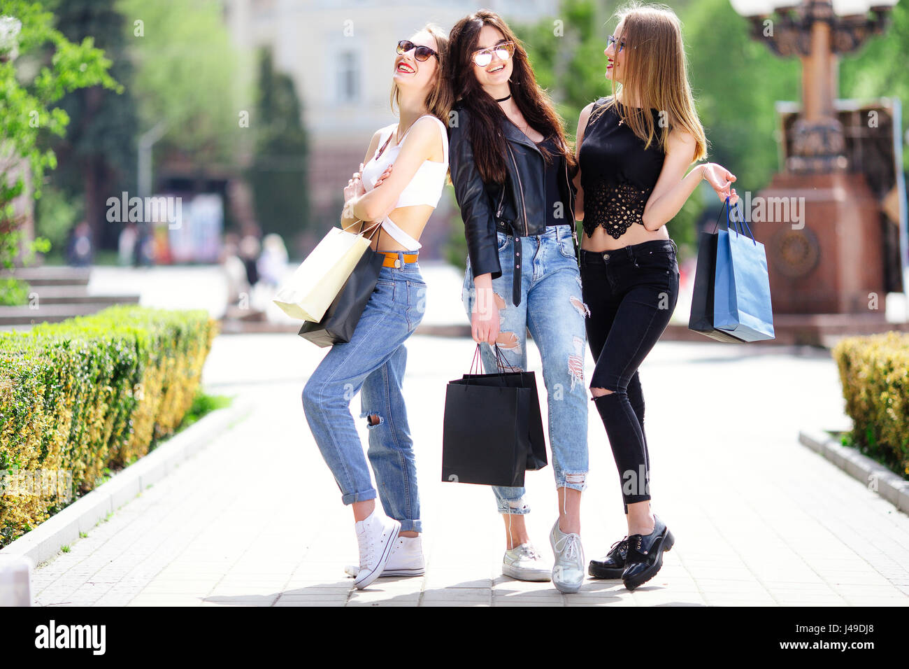 Three girls with shopping bags on park blur background Stock Photo - Alamy