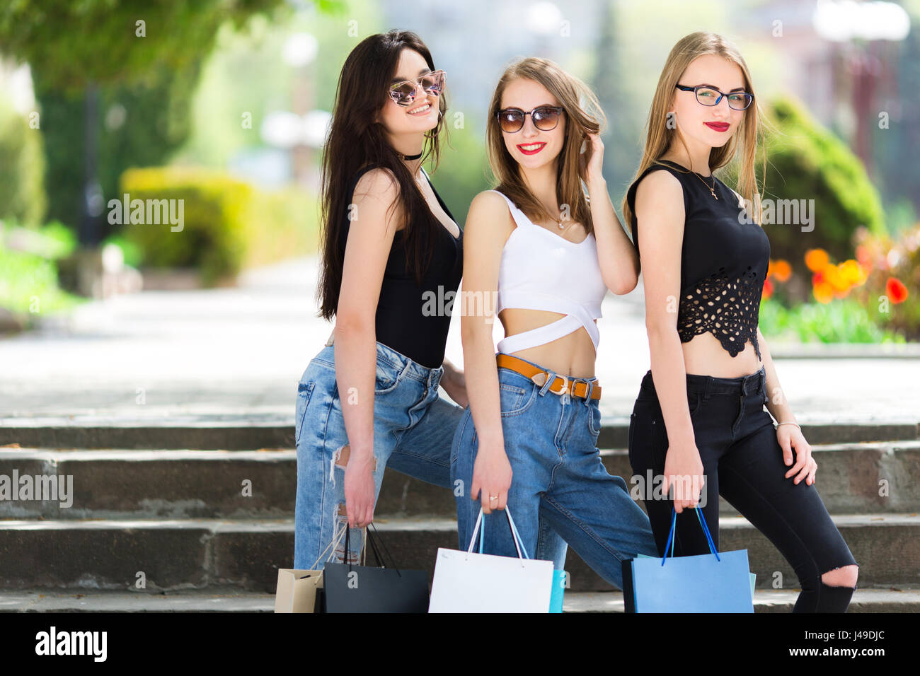 Three girls with shopping bags on park blur background Stock Photo - Alamy