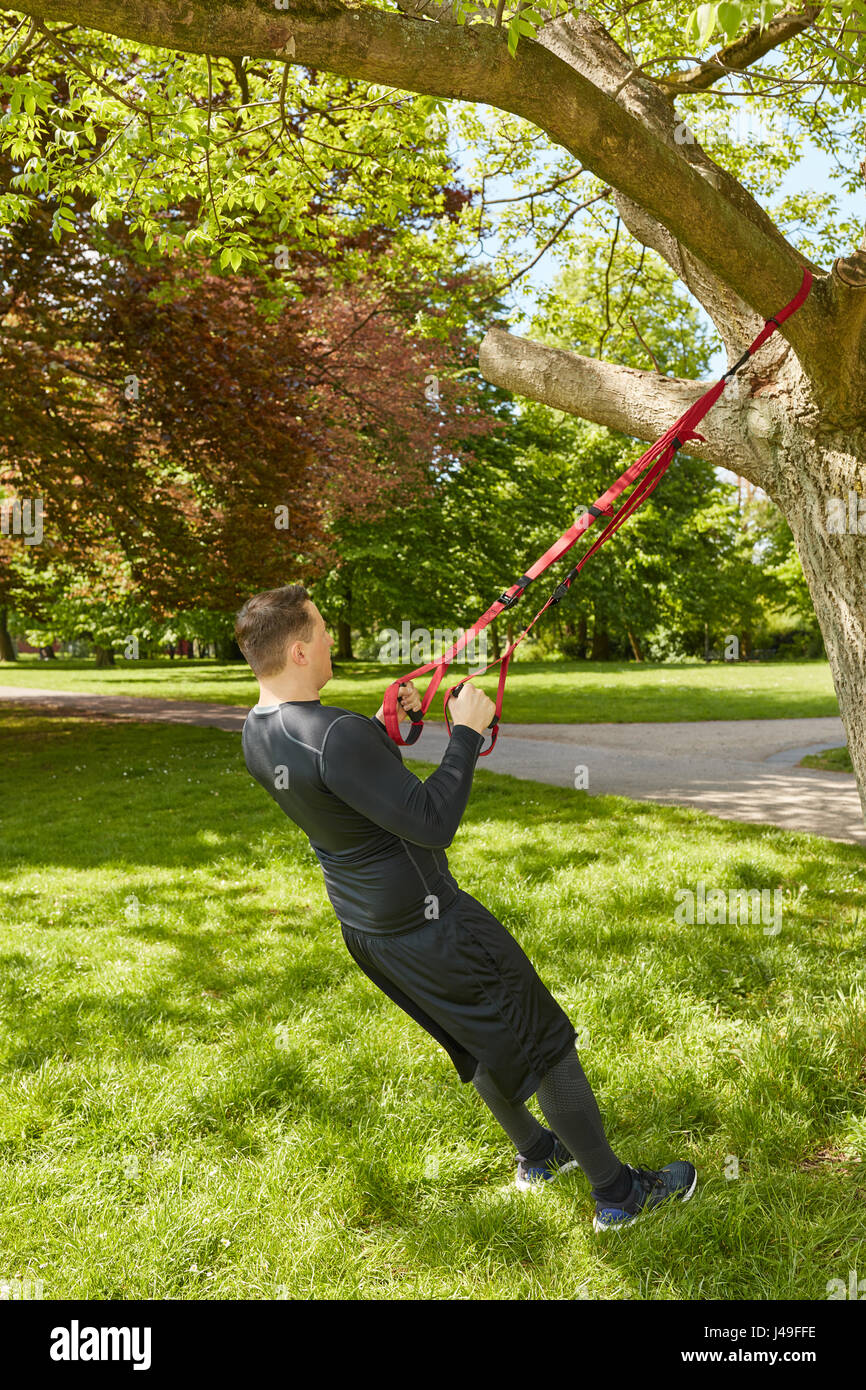 Man practice suspension training at park using tree in summer Stock ...