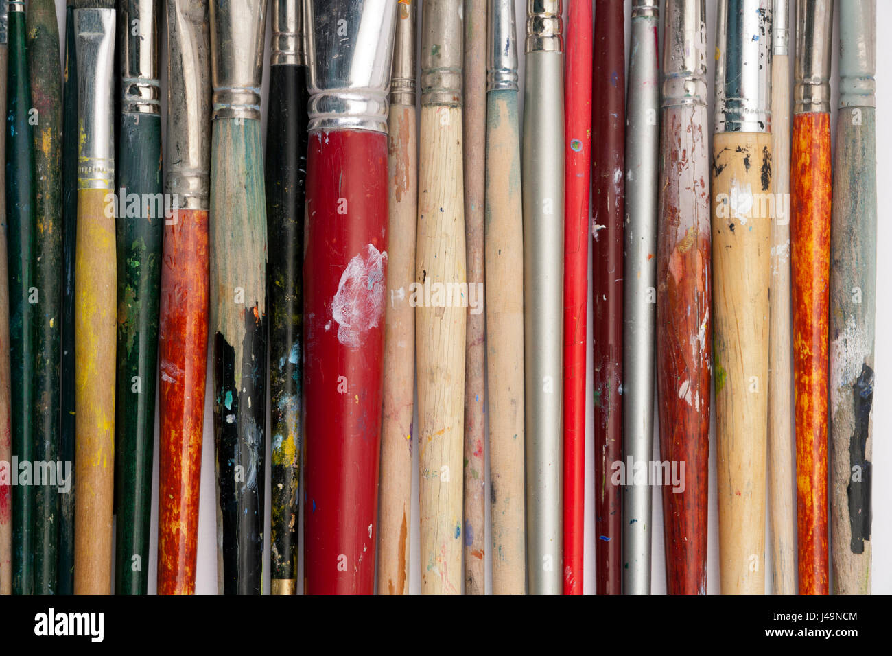 A collection of well used art paint brushes on white paper surface ...
