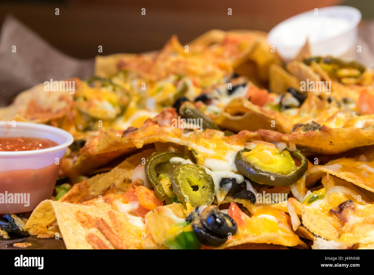 A large plate of nachos, smothered in cheese, veggies and jalapenos ...