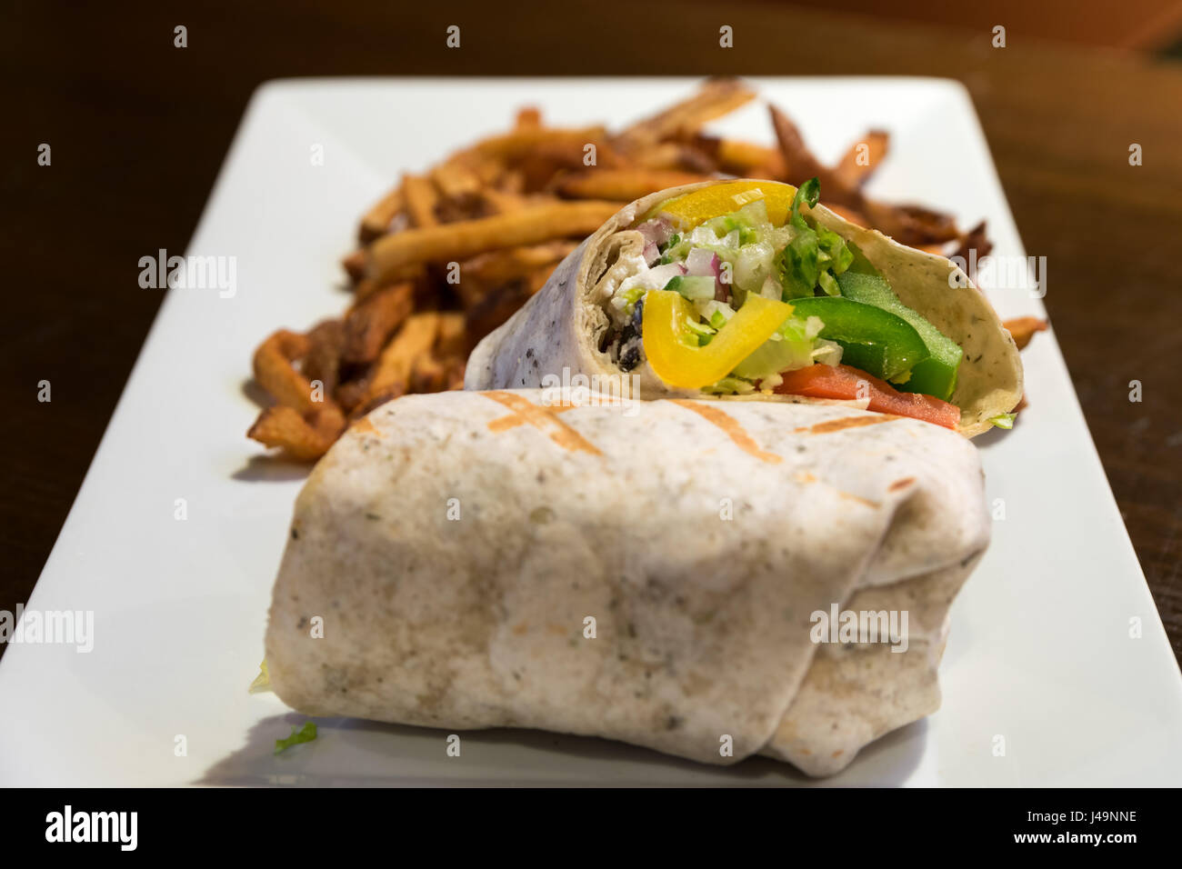 A grilled Greek veggie wrap served with french fries on a white plate ...