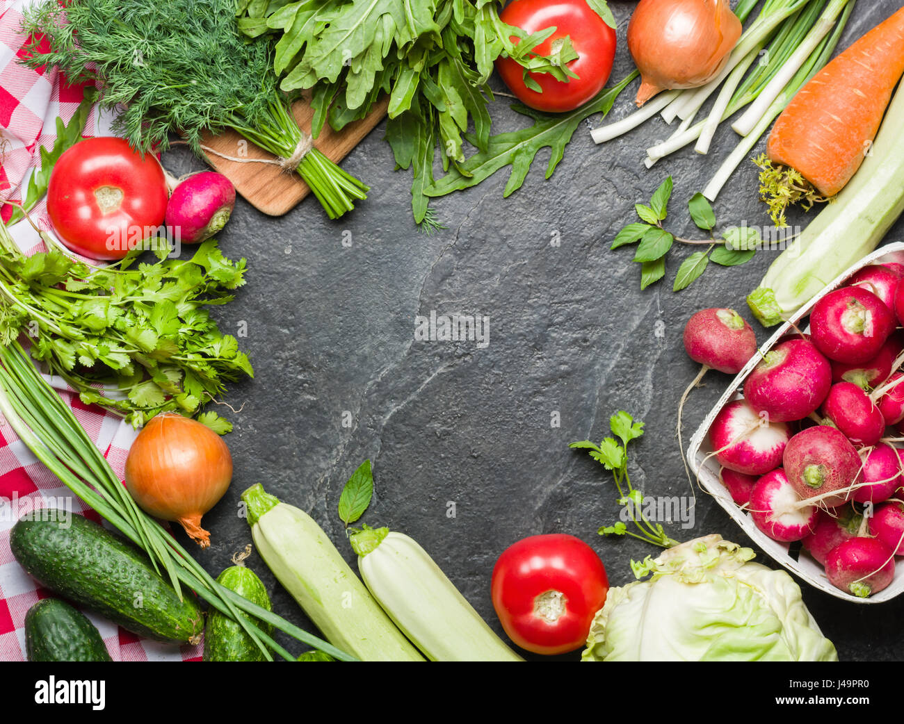 Fresh vegetables and greens in bunches arranged in a frame on a black ...