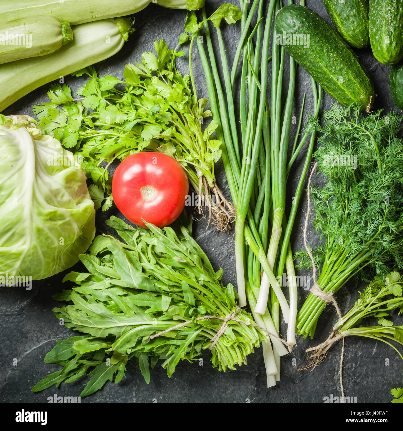 Fresh vegetables and greens in bunches arranged in a frame on a black ...