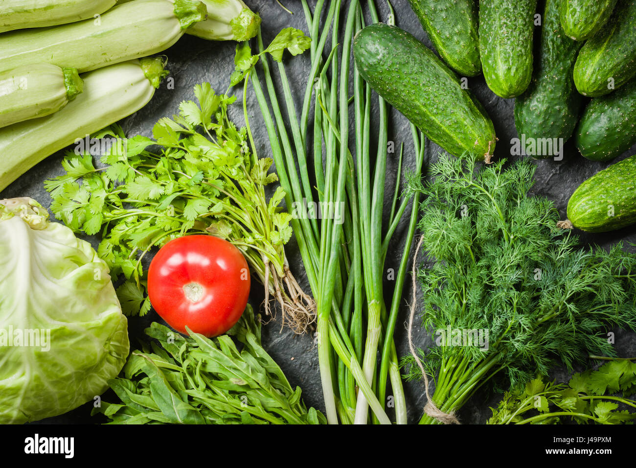 Fresh vegetables and greens in bunches arranged in a frame on a black ...