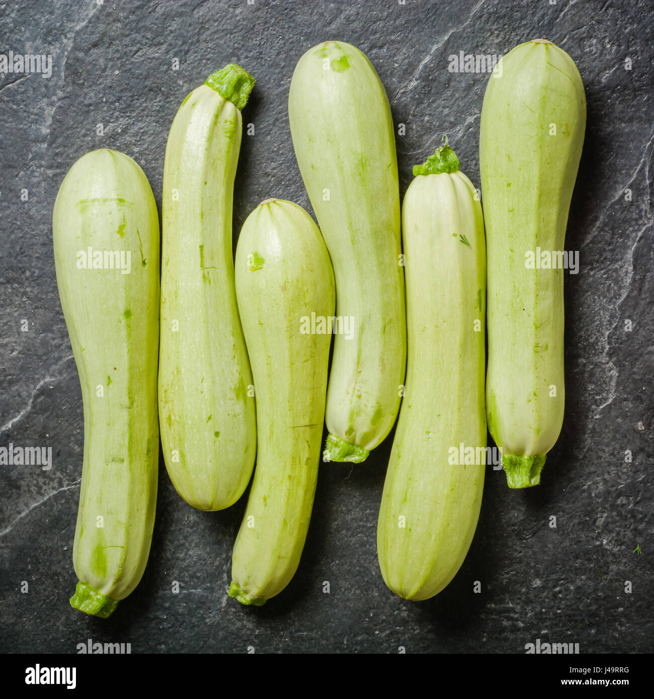 Green young zucchini on a dark stone background. Geometric layout. View ...