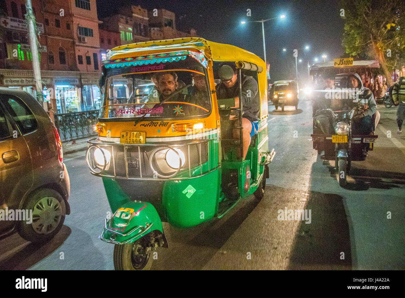 Rickshaws and motorcyclists travel through the streets at nighttime in ...