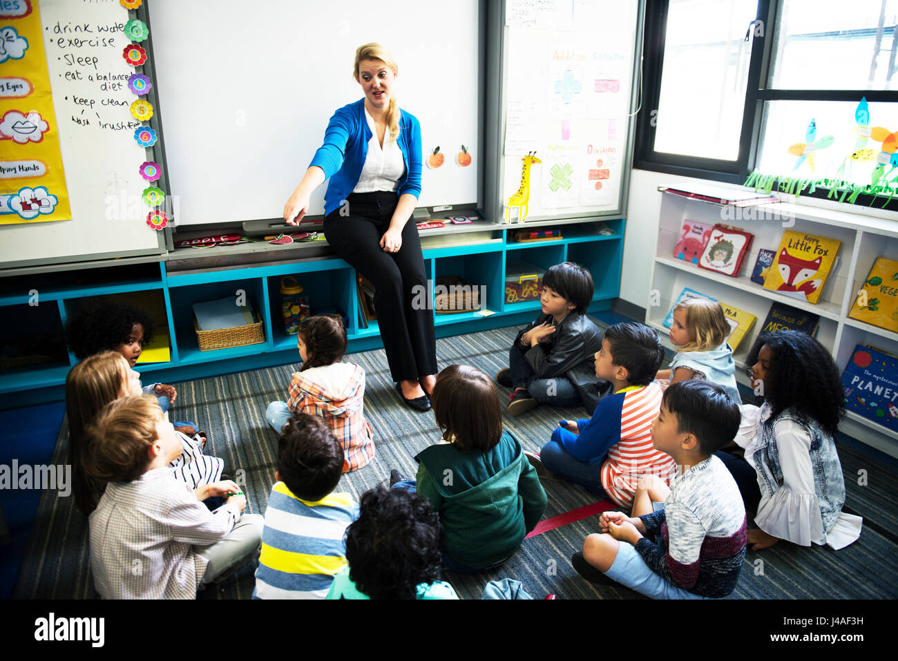 Kindergarten students sitting on the floor listening to teacher Stock ...