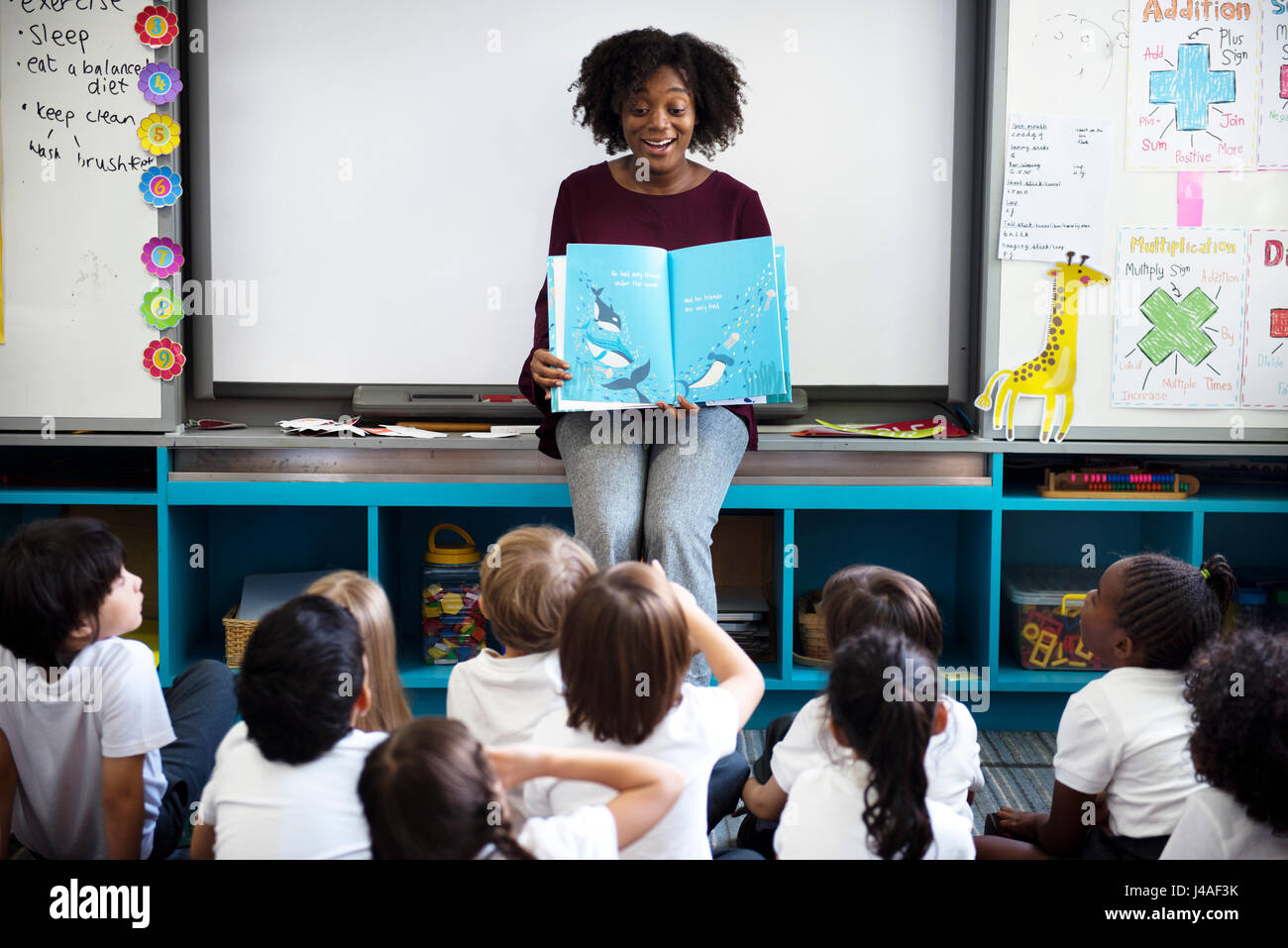 Kindergarten students sitting on the floor listening to story telling ...