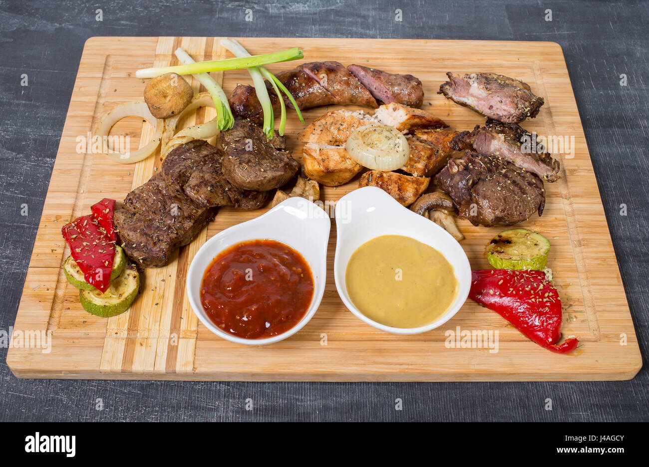 Mixed grilled meats platter with vegetables and sauces. Platter located ...