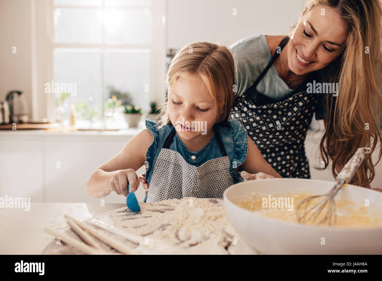 Shot of little girl adding flour to the batter in bowl. Mother teaching ...