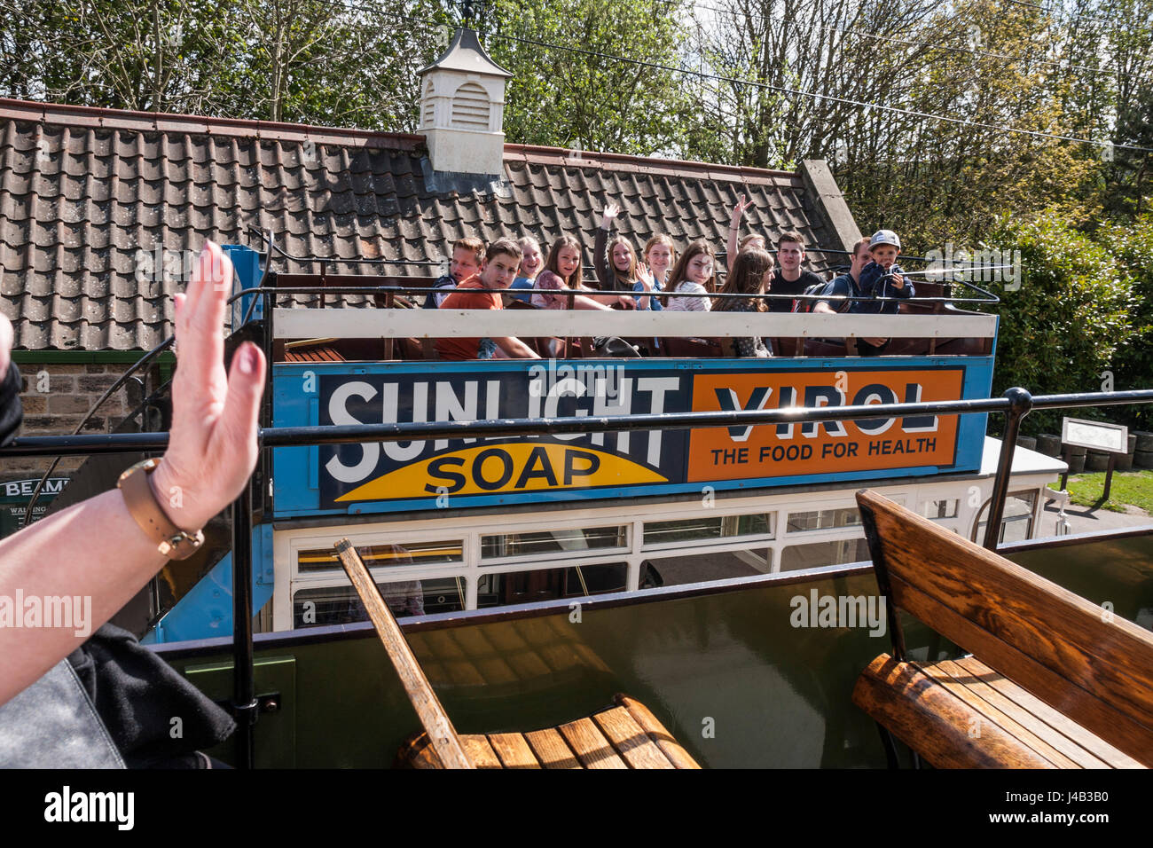Passengers from two open top buses wave to each other as they pass at ...