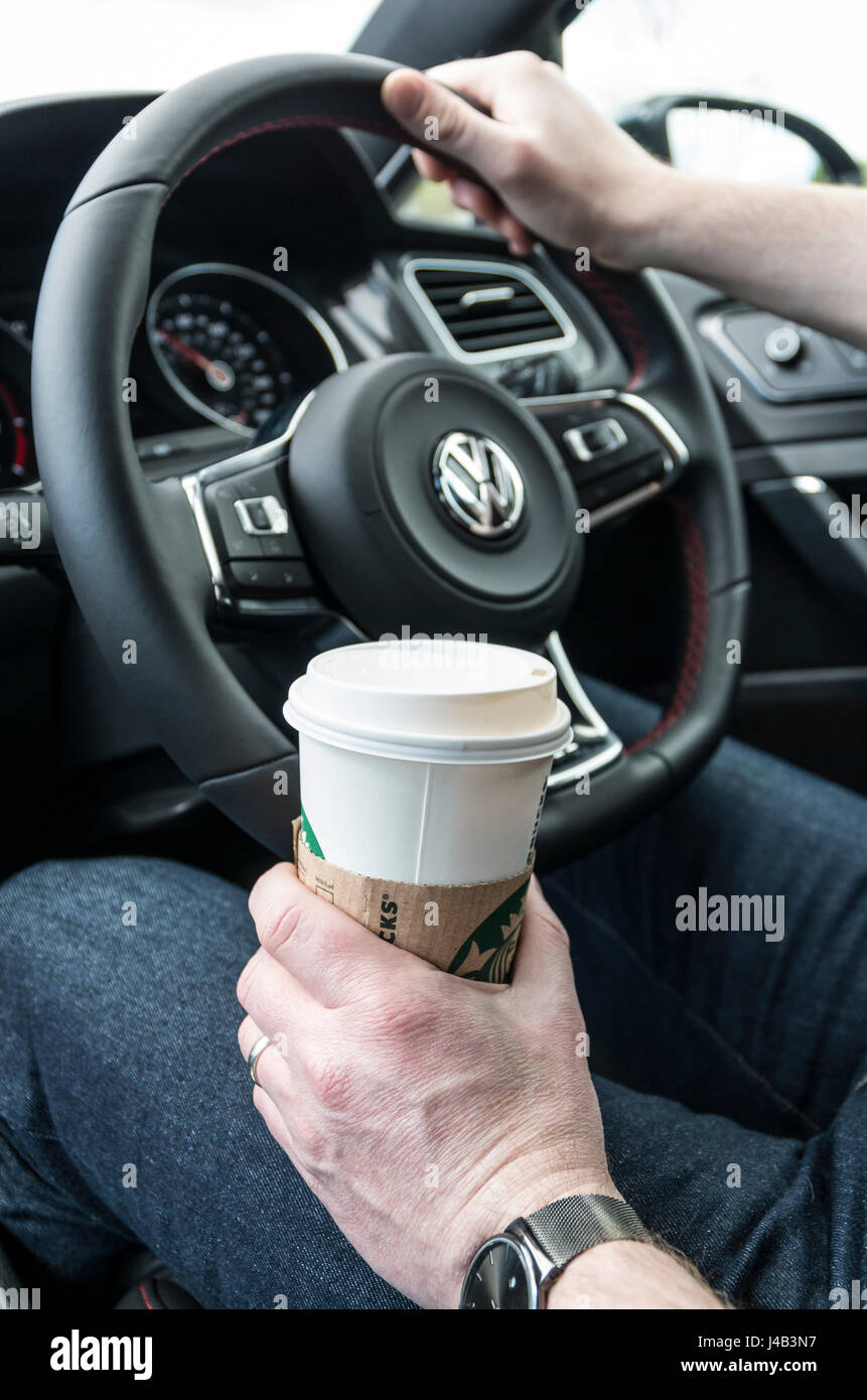 Man driving at wheel of a car with one hand on steering wheel and a ...