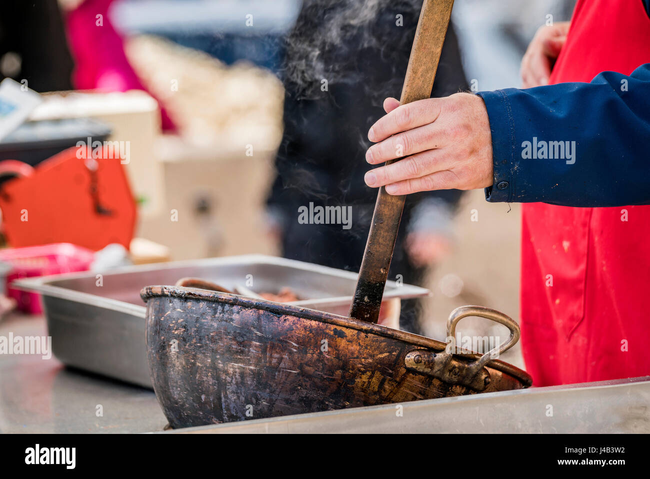 Outdoor kitchen with a man stirring in a hot pot with smoke around in ...