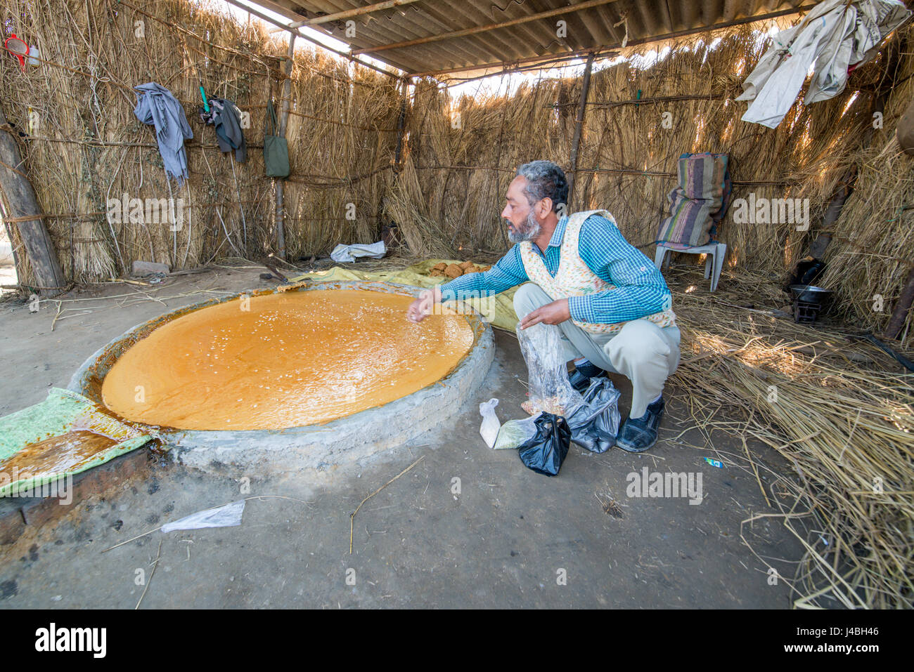 A worker is adding ingredients to a large mix of jaggery (traditional ...