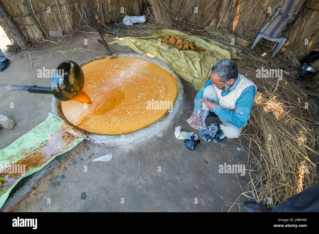 A worker is adding ingredients to a large mix of jaggery (traditional ...
