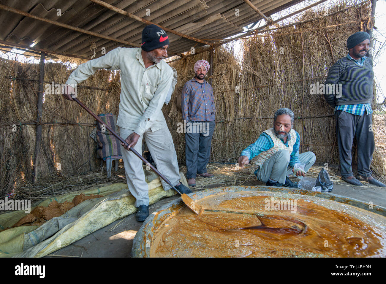 A worker is stirring a large batch of jaggery (traditional cane sugar ...