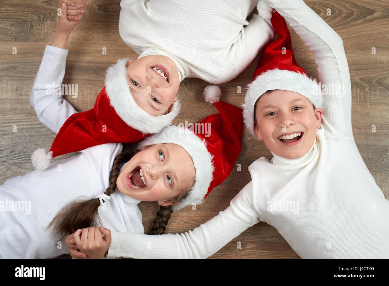 three kids in Santa hats lying on wooden background, having fun and ...
