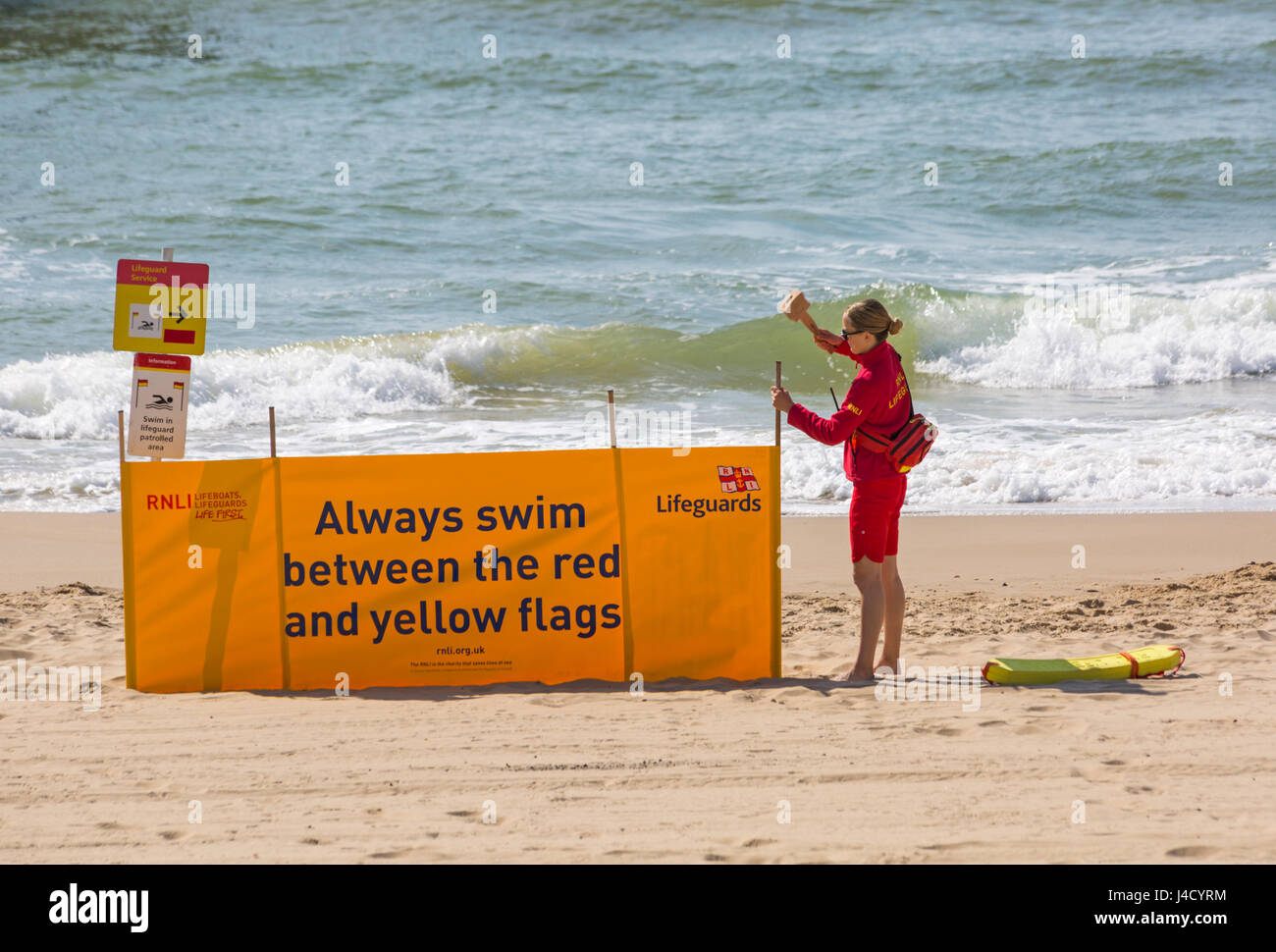 Female RNLI lifeguard putting up safety banner Always swim between the ...