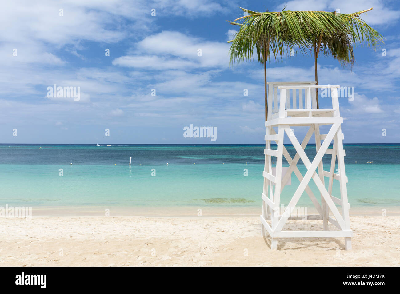 A white lifeguard tower shaded by palm fronds near the tranquil waters ...