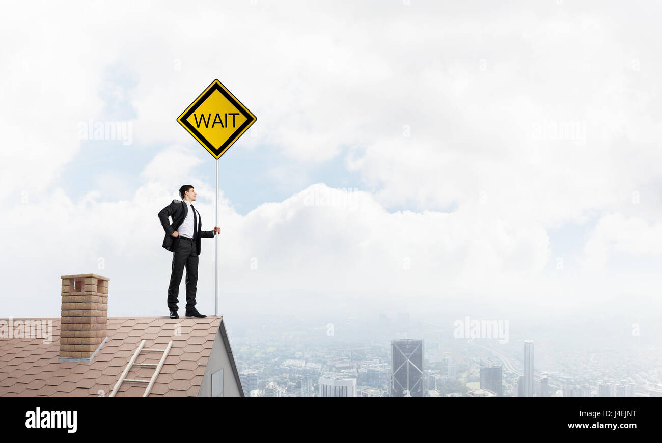 Young businessman on house brick roof holding yellow signboard and ...