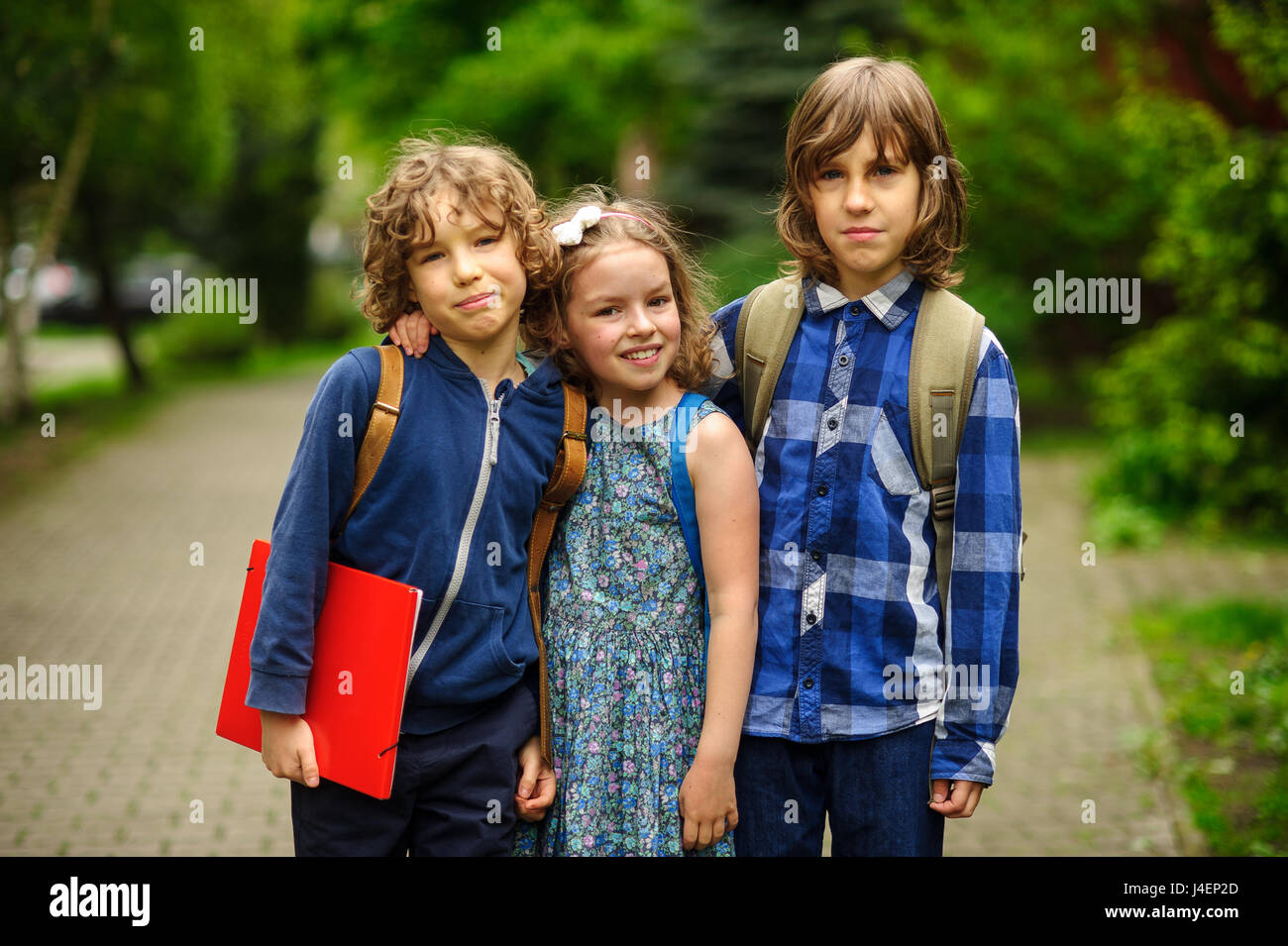 Three little school students, two boys and the girl, stand in an ...