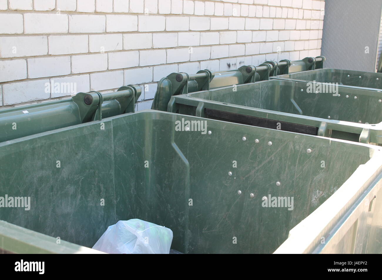 dumpsters standing in front of a white brick wall Stock Photo - Alamy