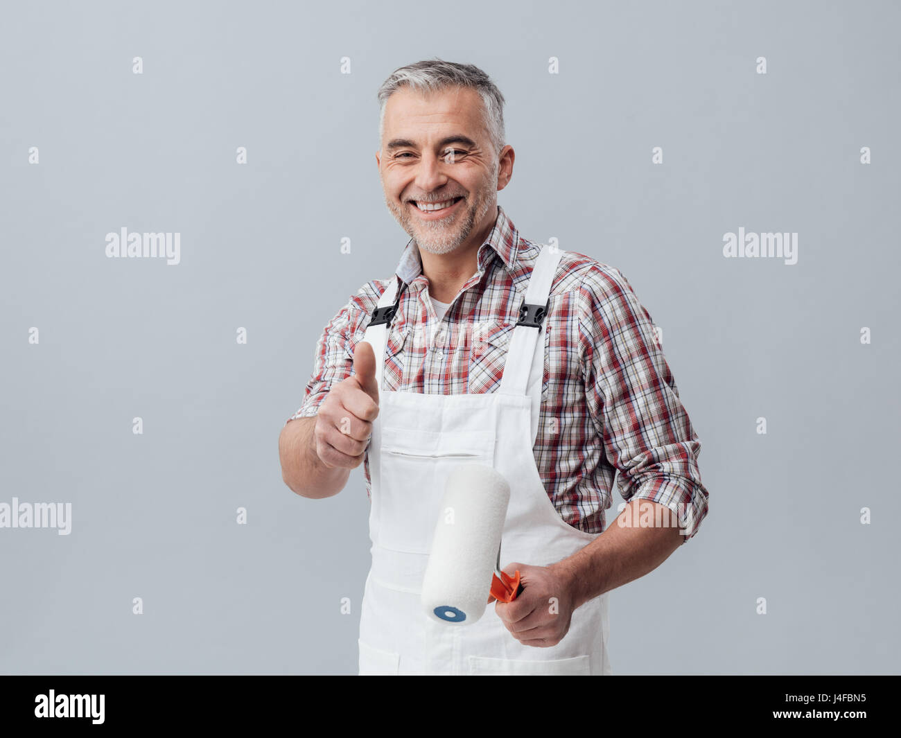Cheerful painter and decorator giving a thumbs up, he is holding a ...