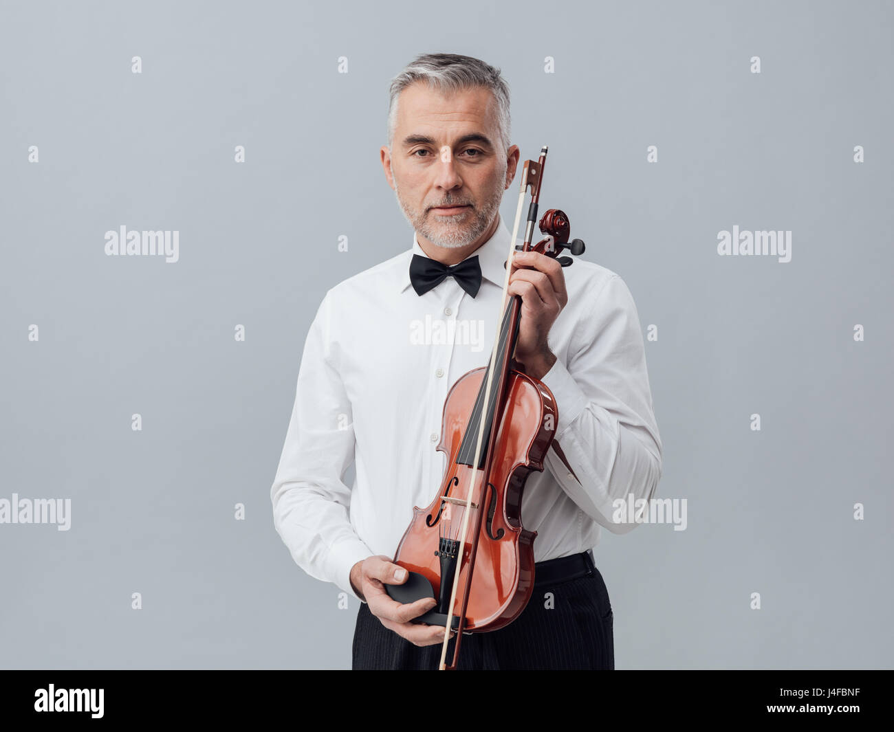 Confident mature musician posing with a violin and looking at camera ...
