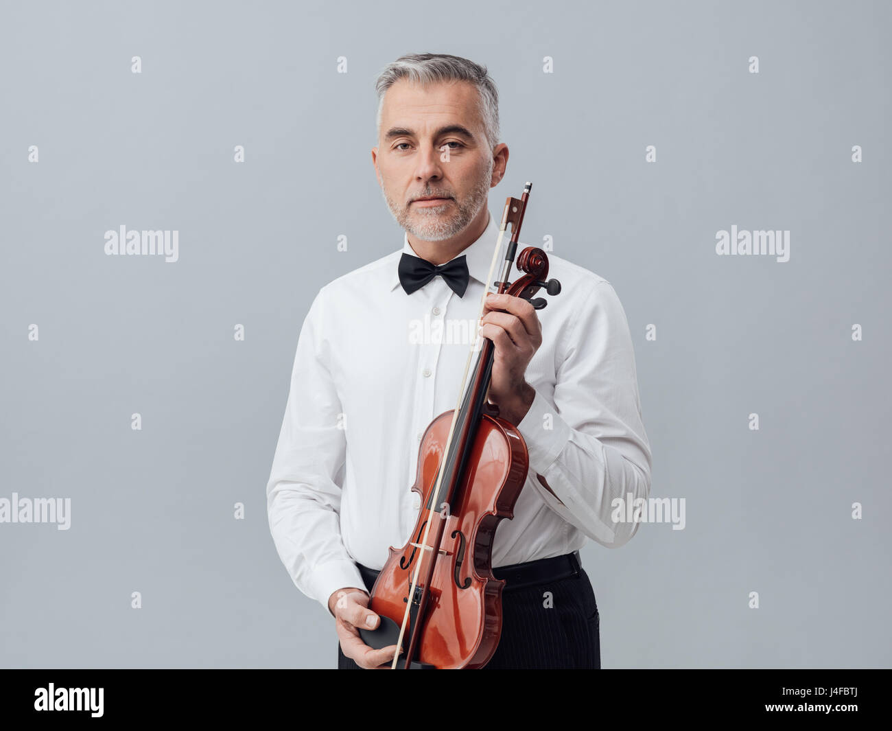 Confident mature musician posing with a violin and looking at camera ...